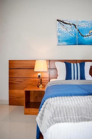 Quarto com cabeceira de madeira, mesa de cabeceira com luminária e cama com travesseiro listrado em azul e branco.