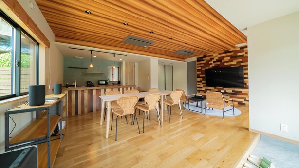 Uma cozinha moderna com teto de madeira, sala de jantar com cadeiras de vime e um espaço de bar.