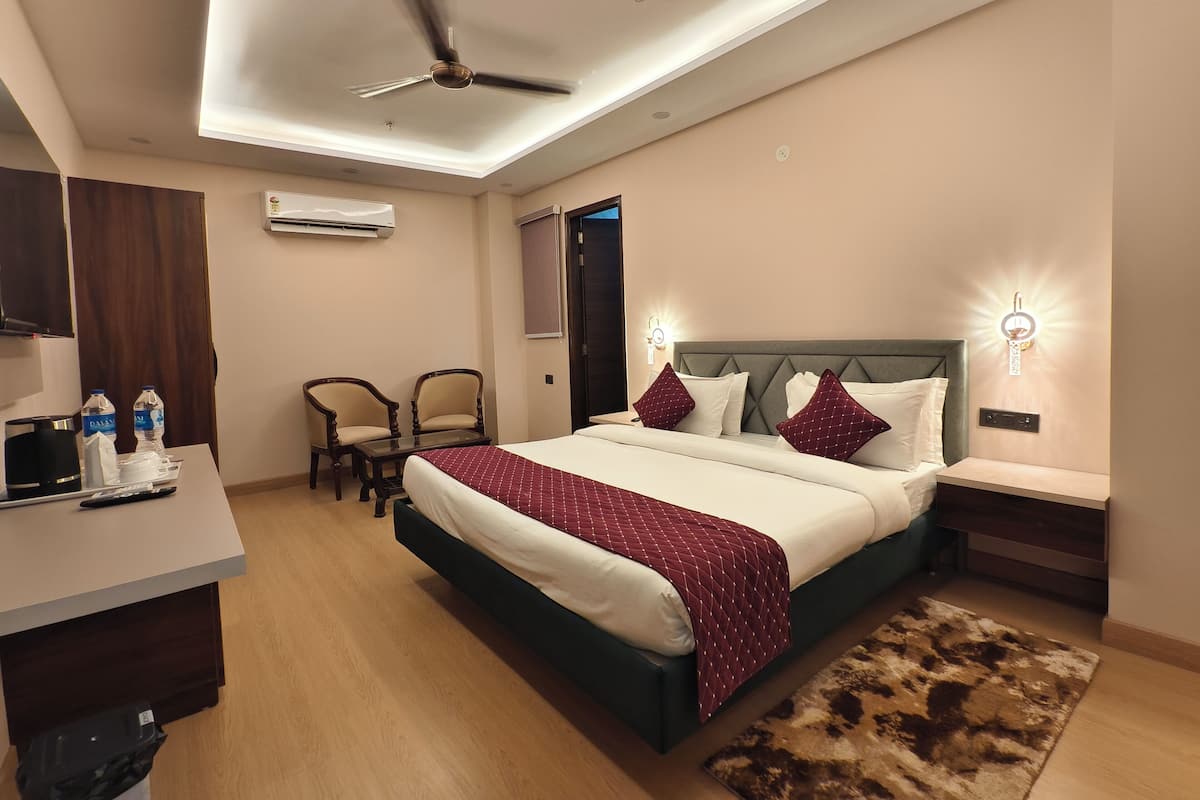Quarto de hotel com uma cama, uma escrivaninha com cadeira, um ventilador de teto e uma luminária fixada na parede.