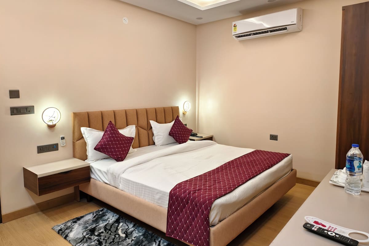 Quarto de hotel com cama, mesas de cabeceira, ar condicionado fixado na parede e um controle remoto sobre a mesa.