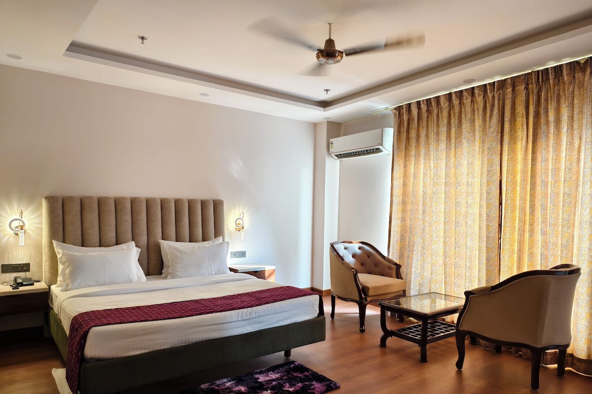 Quarto de hotel com cama, mesas de cabeceira, uma cadeira, uma pequena mesa e um ventilador de teto.