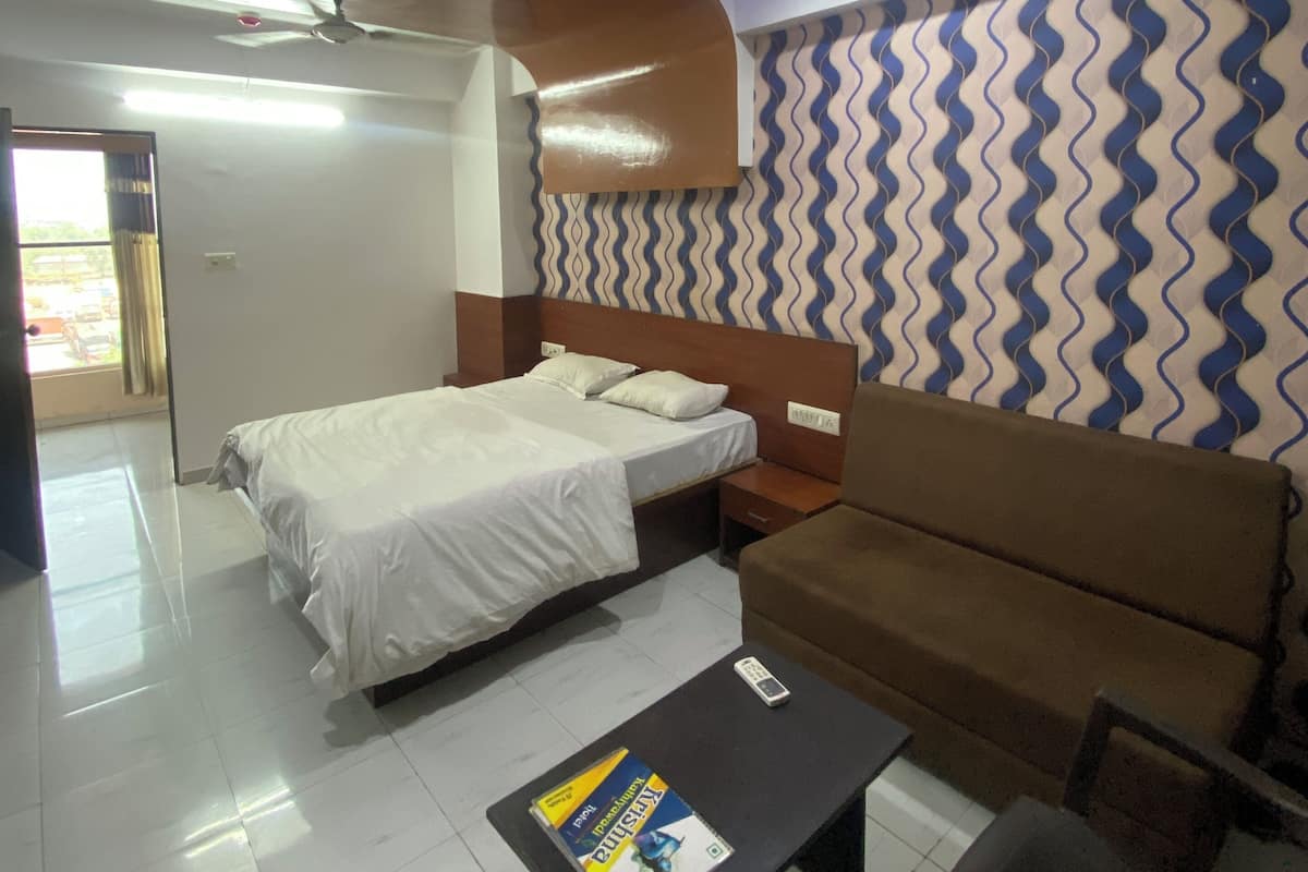 Quarto de hotel com cama, sofá, mesa de centro com uma revista e parede estampada.