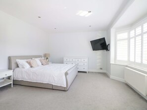 Quarto com cama, mesa de cabeceira, cômoda e televisão na parede.