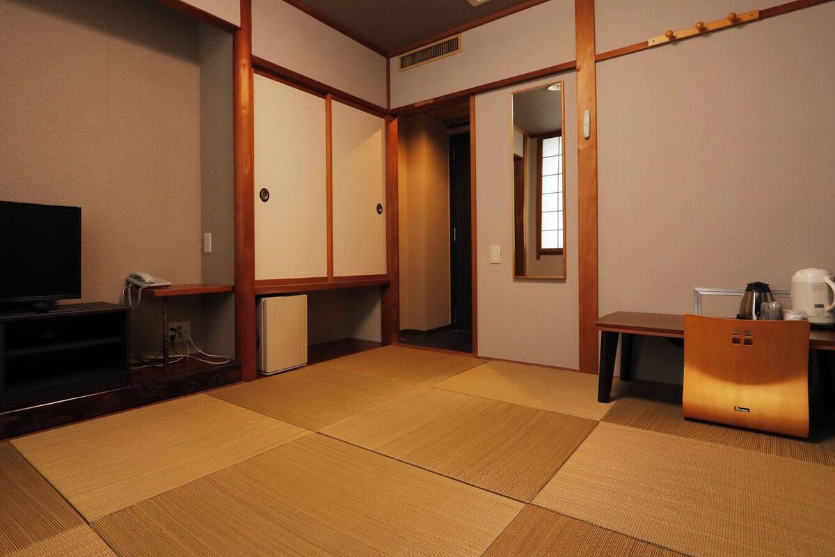 Quarto japonês tradicional com tatames, televisão, pequena geladeira e mesa com chaleira e xícaras.