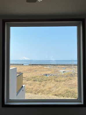 Janela com vista para uma praia, uma montanha ao longe e um cais.