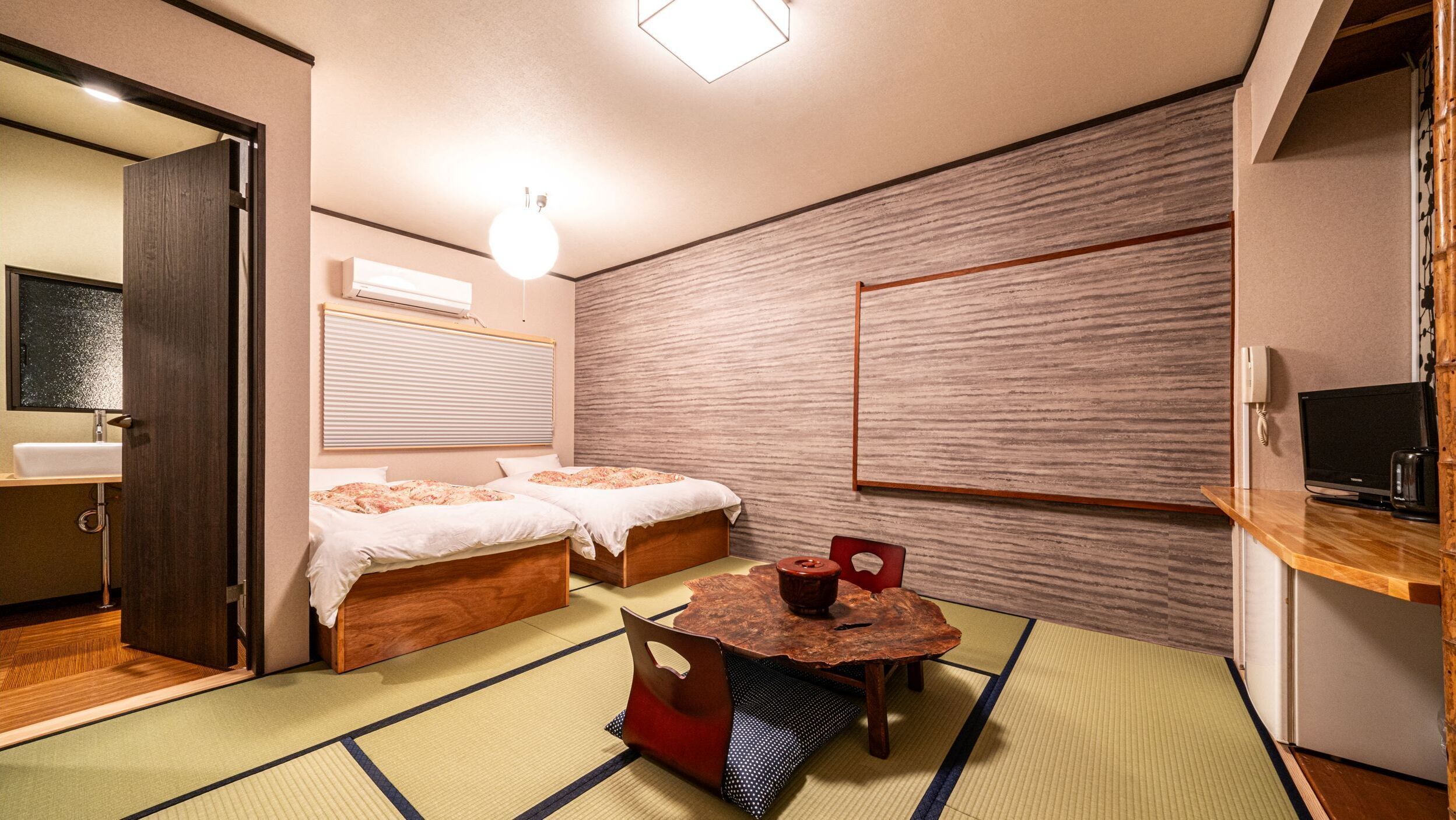 Quarto com duas camas, uma mesinha, televisão e banheiro.