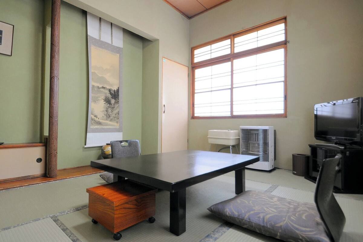 Um quarto com uma mesa, uma cadeira, uma televisão e uma janela.