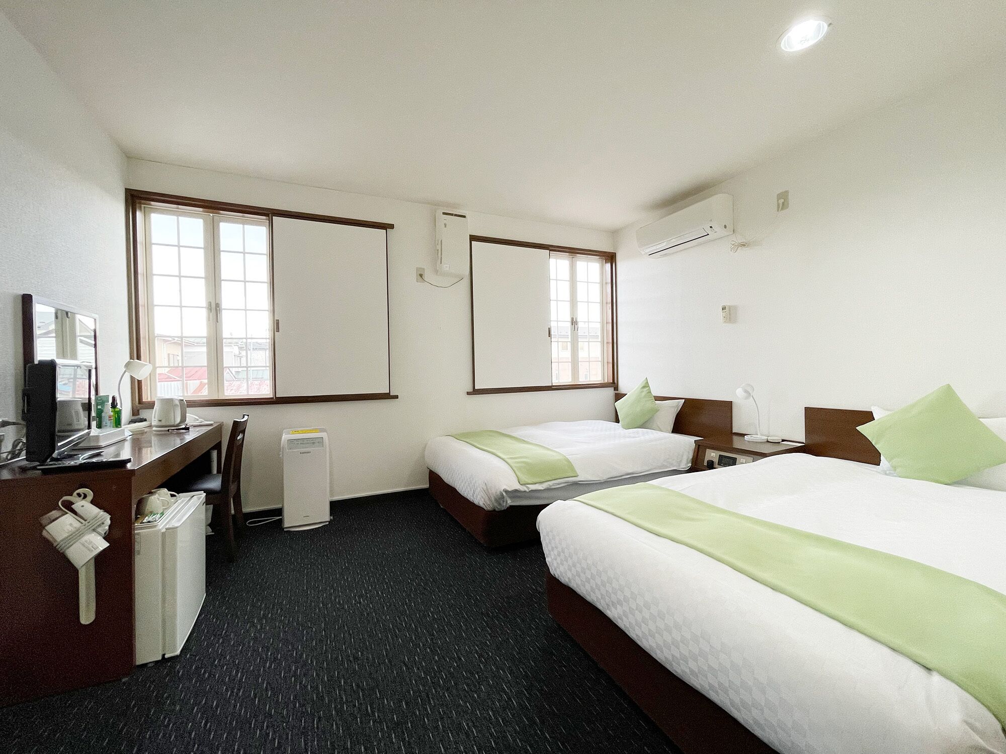 Quarto de hotel com duas camas, uma escrivaninha com computador, uma cadeira, televisão e uma janela.