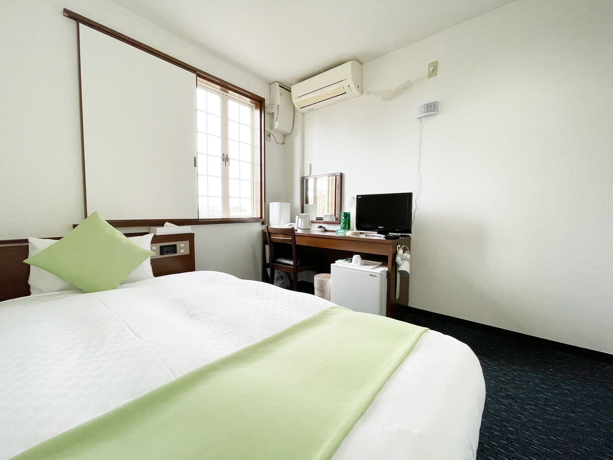 Quarto de hotel com cama, secretária com computador, televisão e aparelho de ar condicionado.