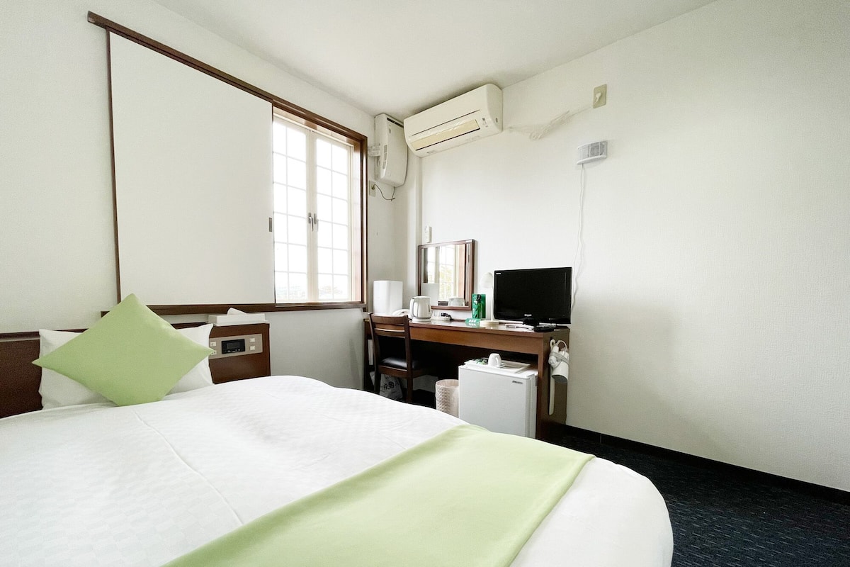 Quarto de hotel com cama, secretária com computador, televisão e aparelho de ar condicionado.