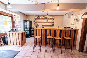 Uma área de bar com banquetas de madeira, balcão e prateleiras cheias de garrafas.