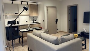 Um espaço de estar moderno com cozinha compacta, sofá, escrivaninha com cadeira e TV fixada na parede.