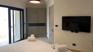 Quarto de hotel com cama, televisão fixada na parede, porta deslizante e luminária pendente vermelha.