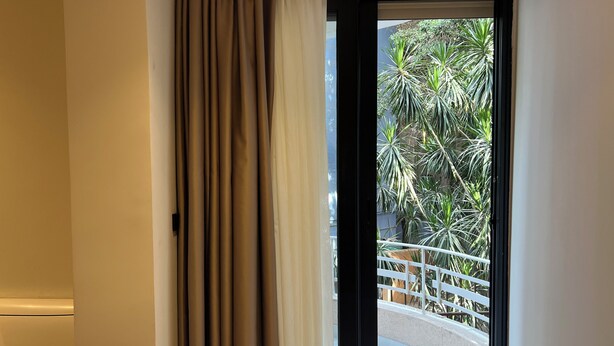 Quarto com porta de vidro deslizante que dá para uma varanda com grades brancas e plantas verdes.