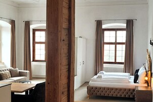 Quarto de hotel com cama, sofá, escrivaninha e janela com cortinas.