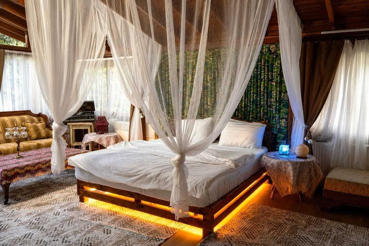Quarto com cama de dossel, sofá, mesinha e mesa de cabeceira.