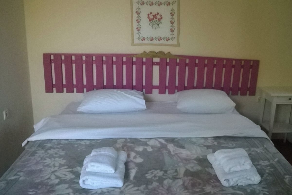 Cama com colcha estampada floral, duas almofadas e duas toalhas dobradas.