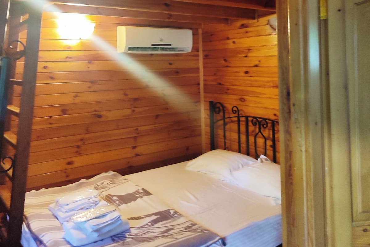 Quarto de cabana de madeira com cama, ar-condicionado fixado na parede e uma escada.