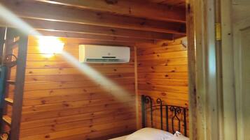 Quarto de cabana de madeira com cama, ar-condicionado fixado na parede e uma escada.