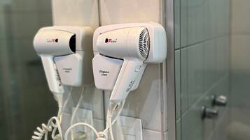 Uma casa de banho com dois secadores de cabelo brancos fixados na parede, um sinal com texto e um chão em azulejos.