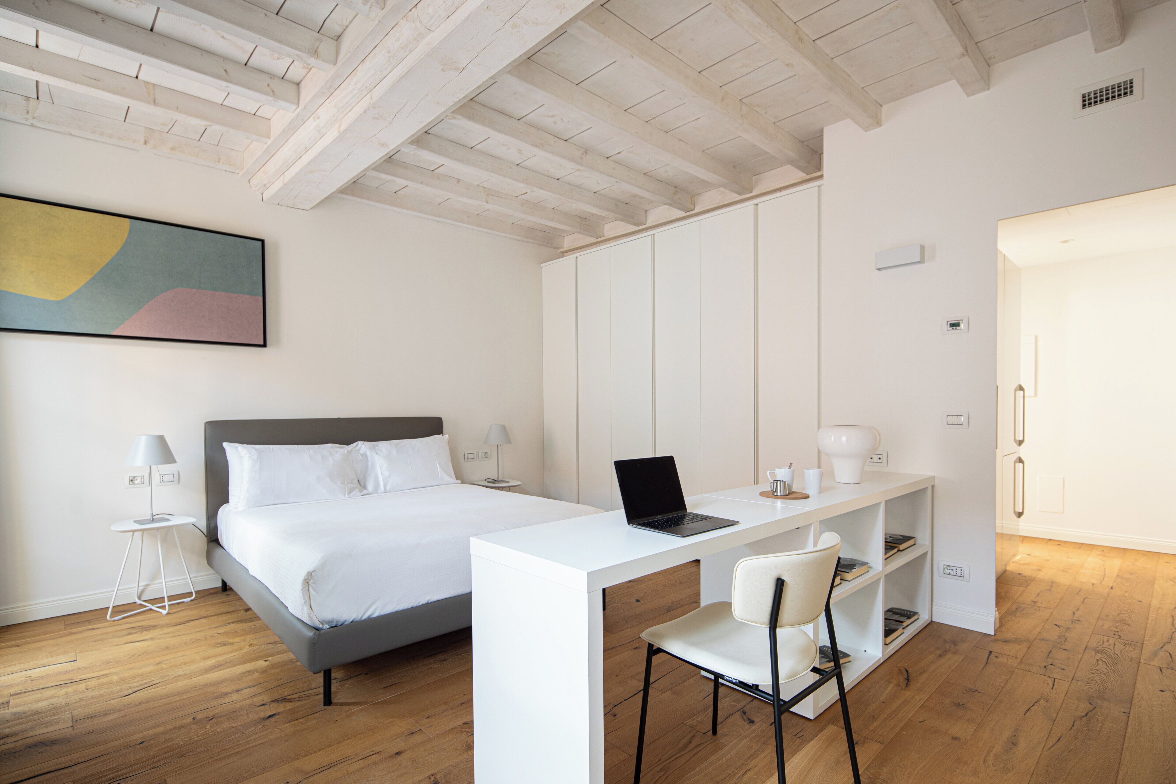 Um quarto moderno com uma cama, uma escrivaninha com um laptop, uma cadeira e uma mesa de cabeceira.