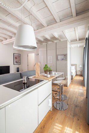 Uma cozinha moderna com uma ilha central, uma área de jantar com um banco alto e uma sala de estar com sofá e televisão.