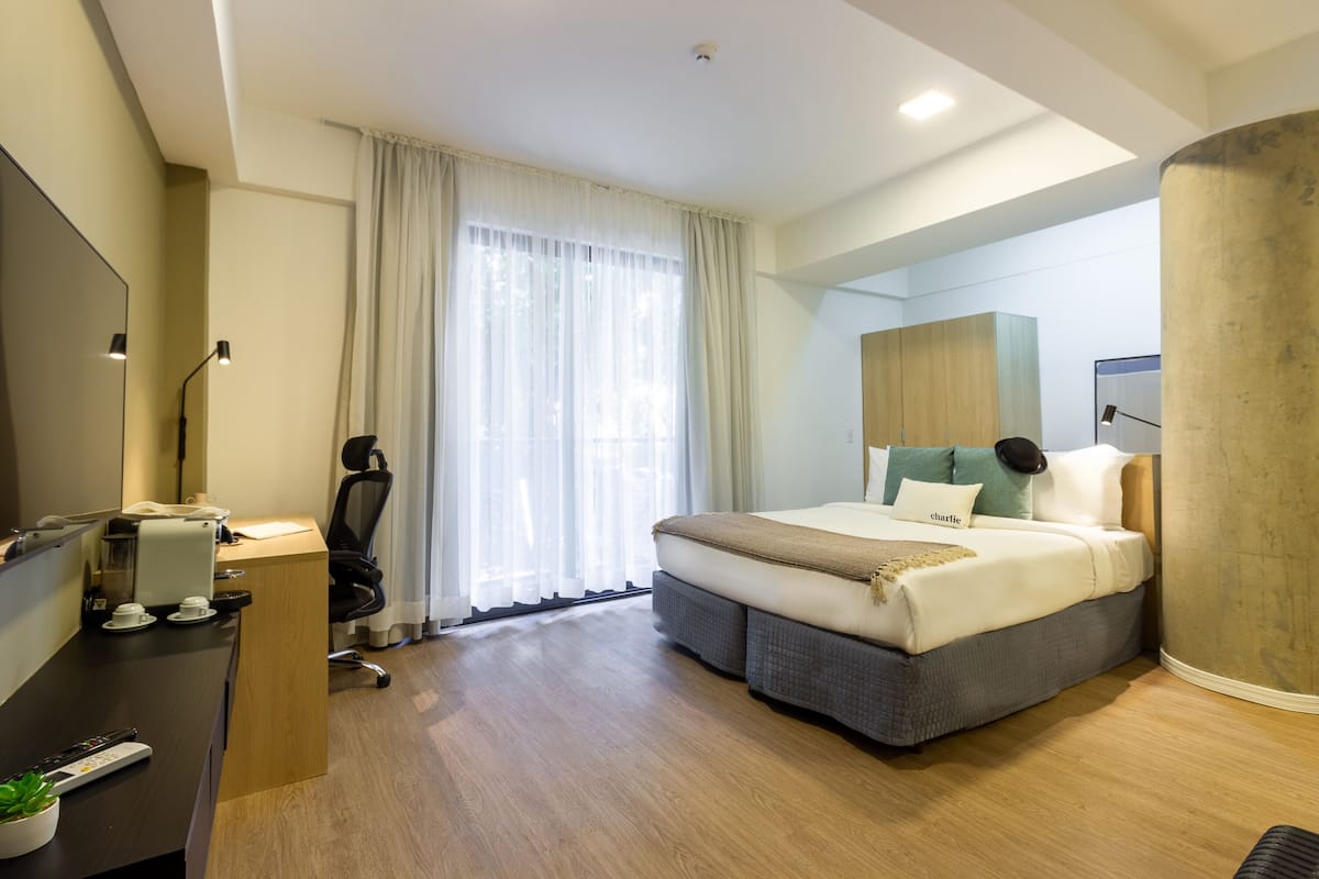 Quarto de hotel com cama, escrivaninha, cadeira e televisão.