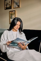 Uma pessoa sentada em um sofá preto lendo um livro.