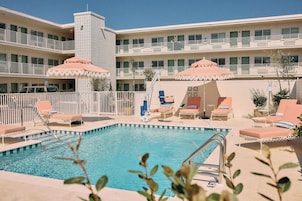Área de piscina de hotel com várias espreguiçadeiras, guarda-sóis e uma piscina azul cristalina.