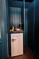 Uma kitchenette compacta com geladeira branca, cafeteira e uma pequena caixa de madeira em cima.
