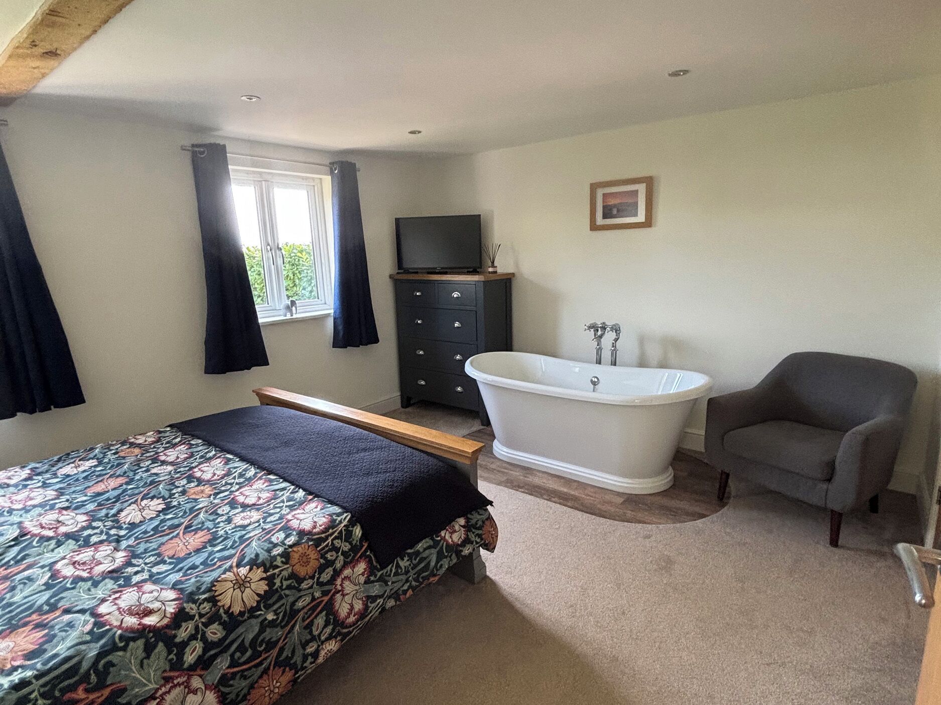 Quarto com cama, banheira, cadeira, cômoda e televisão.