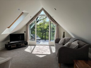 Quarto moderno estilo loft com claraboia, janela ampla, sofá e televisão.