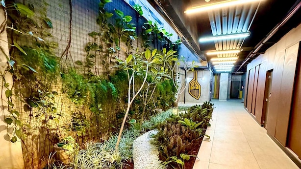 Um corredor com jardim integrado, piso em azulejo e teto com tubulações aparentes.