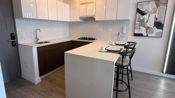 Cozinha moderna com armários brancos, uma ilha central, banquetas, fogão embutido e luminária pendente.