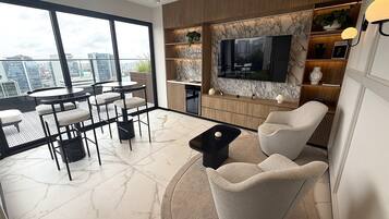 Uma sala de estar moderna com uma televisão grande, assentos confortáveis, um espaço de refeições e vista para a cidade.