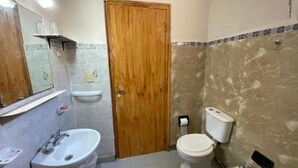 Uma casa de banho com porta de madeira, pia, sanita e bidé.