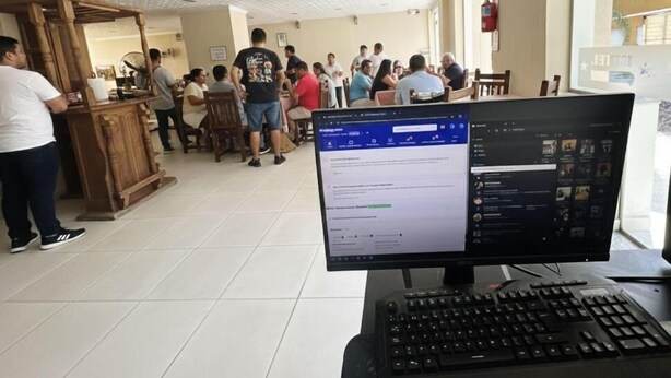 Interior de restaurante com piso de azulejos, mobiliário de madeira e um monitor de computador exibindo uma página web.