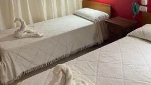 Quarto de hotel com duas camas, parede decorada em vermelho, mesa de cabeceira e luminária fixada na parede.