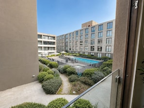 Um edifício moderno com piscina, rodeado por vegetação bem cuidada e um céu claro.