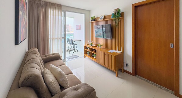 Uma sala de estar com sofá, televisão sobre suporte de madeira, porta de correr de vidro e porta de madeira.
