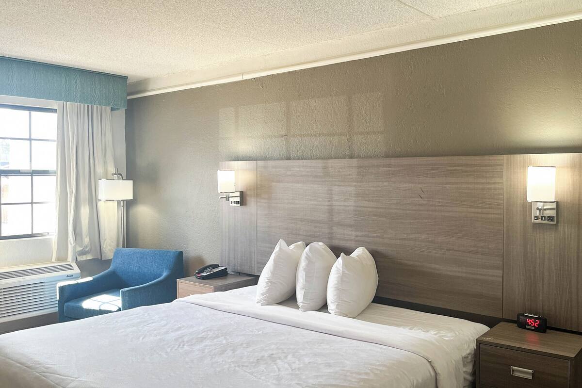 Quarto de hotel com uma cama grande, abajures, uma mesa com telefone e uma cadeira.