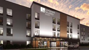 Um edifício de hotel moderno com uma placa grande Livsmart Studios, várias janelas e uma entrada bem iluminada.