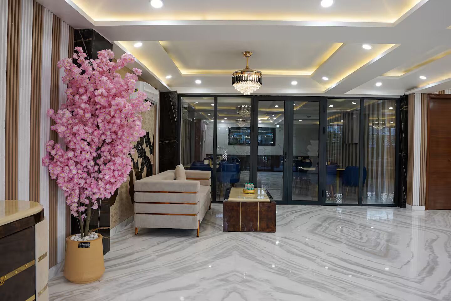 Um hall moderno com piso de mármore, um arranjo grande de flor cor-de-rosa artificial, um sofá e um candelabro.