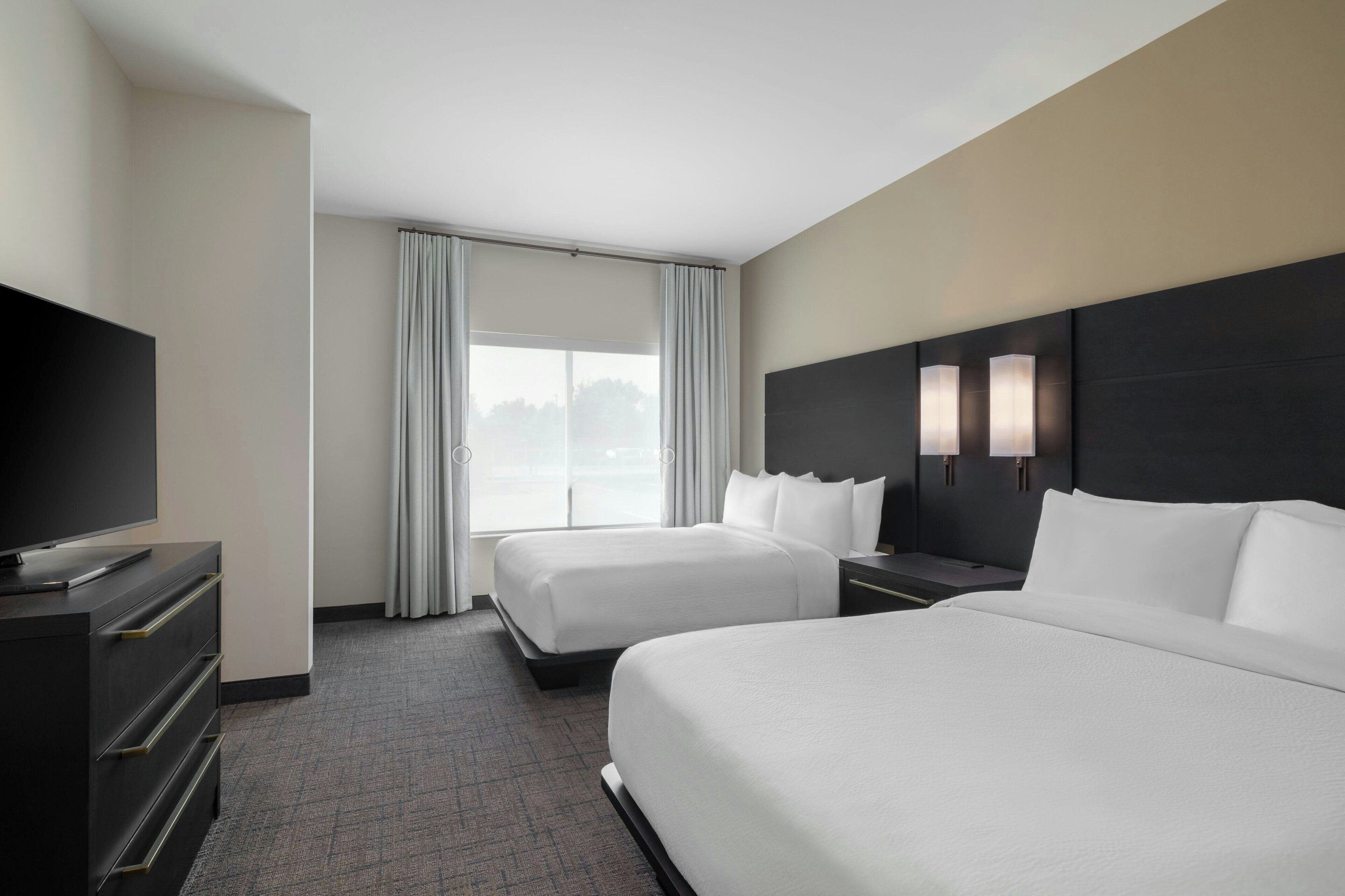 Quarto de hotel com duas camas, televisão de tela plana, cômoda e uma janela grande com cortinas.