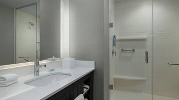 Uma casa de banho moderna com uma pia branca, um espelho, um porta-toalhas e uma cabine de duche com vidro.