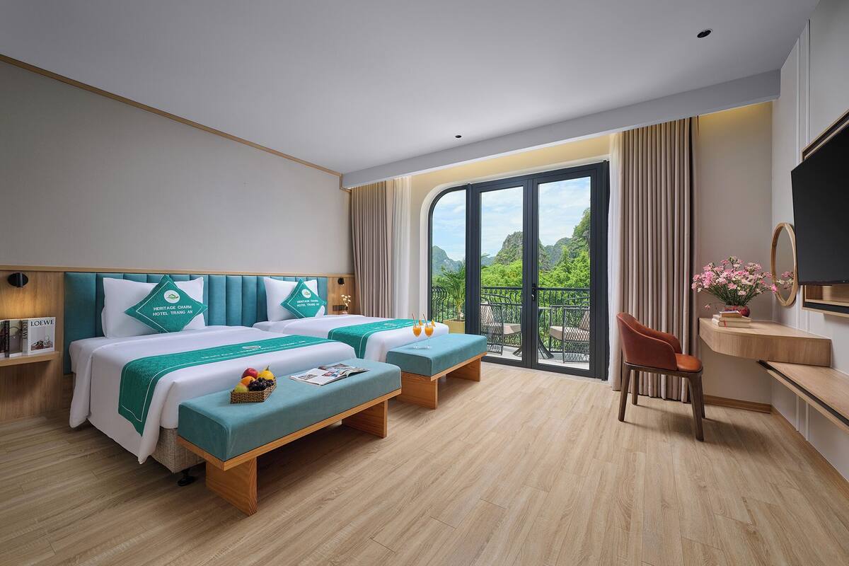 Quarto de hotel com cama, duas mesas de cabeceira, uma cadeira, televisão e varanda com vista.