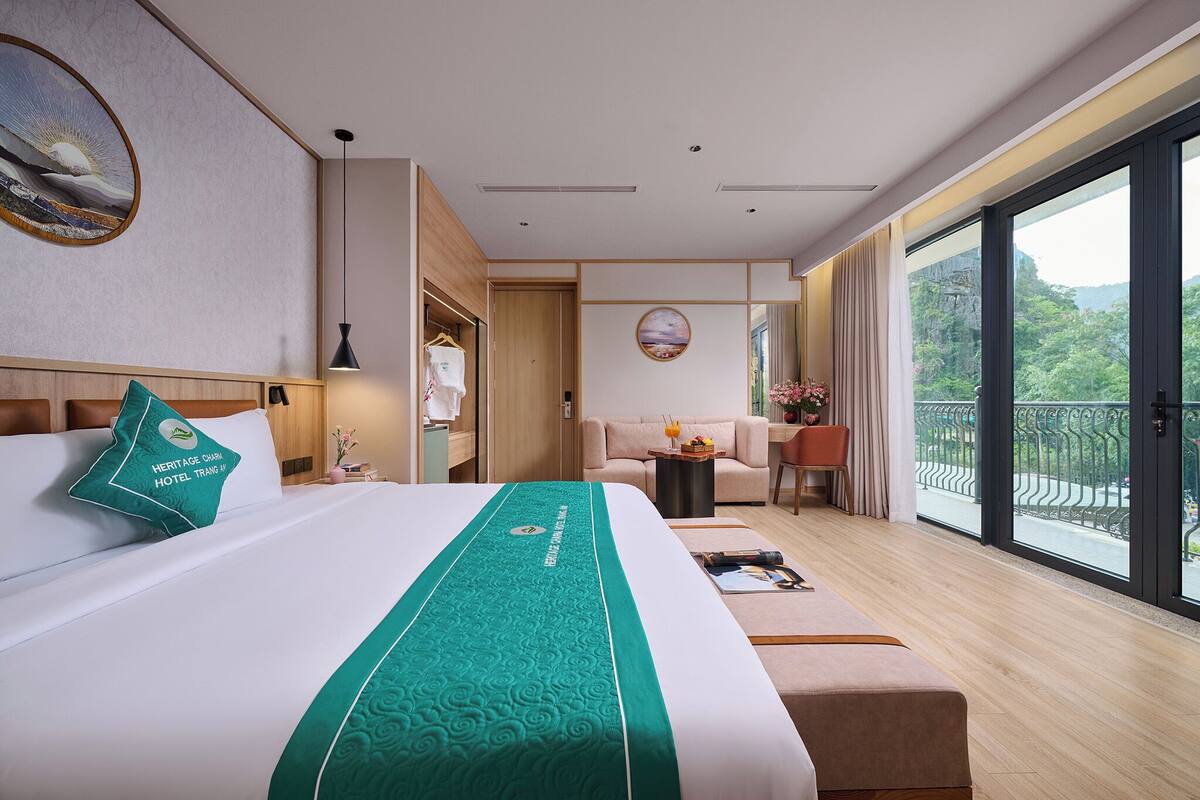 Quarto de hotel com uma cama grande, área de estar, vista para o exterior e porta que dá para uma varanda.