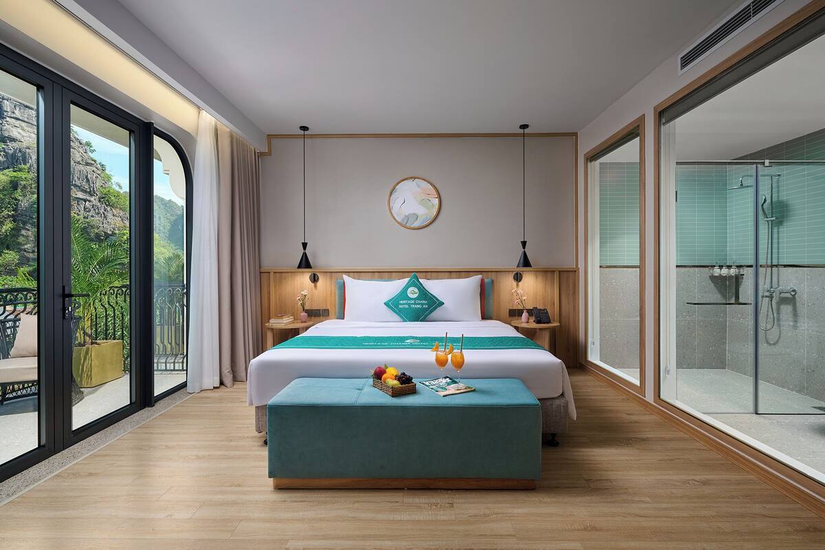 Quarto de hotel com uma cama grande, mesa de cabeceira, chuveiro de vidro e varanda com vista para uma montanha.