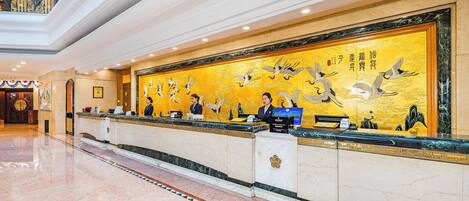Uma área de recepção de hotel com piso de mármore, balcão de atendimento e um grande mural na parede.