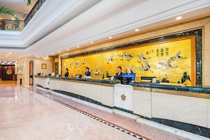 Uma área de recepção de hotel com piso de mármore, balcão de atendimento e um grande mural na parede.